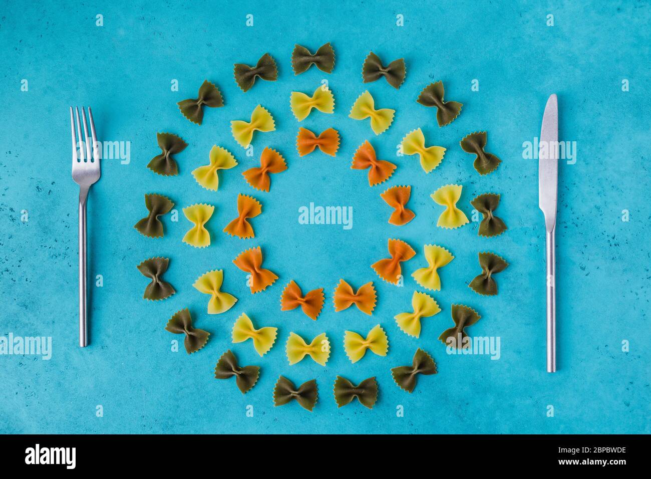 raw colourful pasta rounded as plate with fork and knife Stock Photo ...