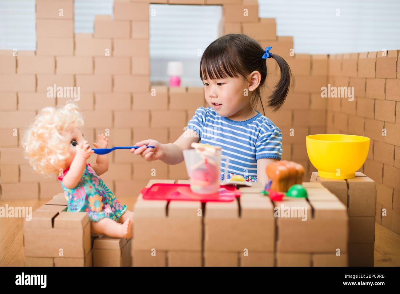 toddler girl pretend play baby care in a carton house Stock Photo - Alamy