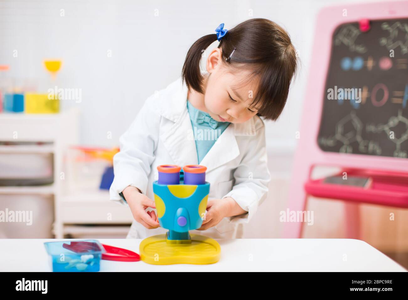 toddler girl pretend play scientist role at home against white ...