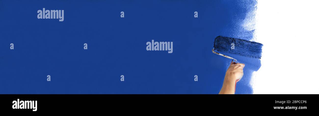 Human hand with large roller of paint begins to paint a white wall ...