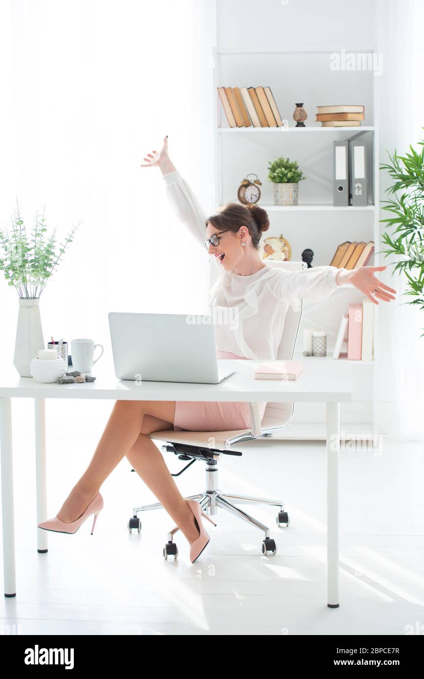 A young woman in the office smiles and screams cheers from happiness ...
