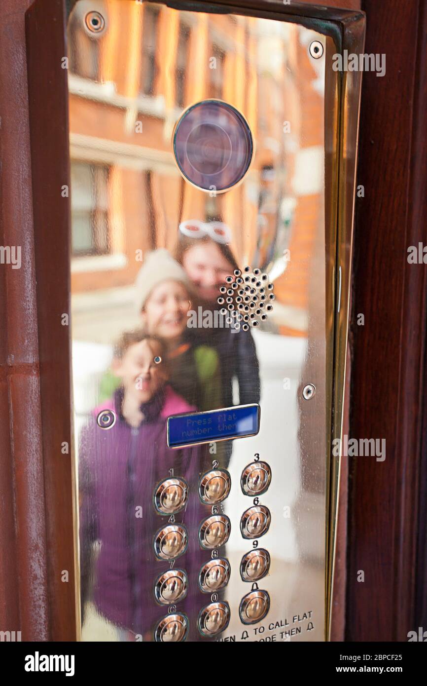 Three kids of varying ages comically reflected in an apartment intercom ...