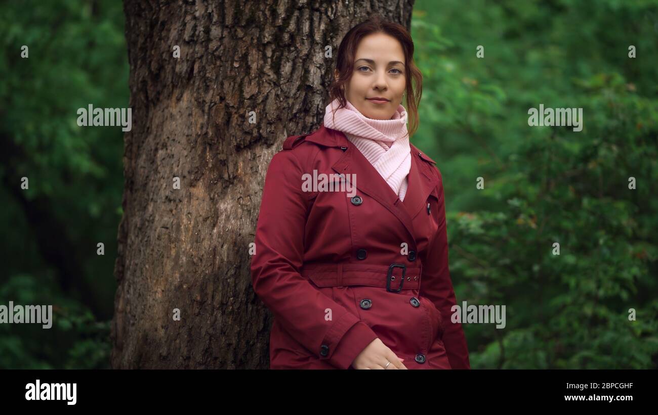 Portrait of young pretty woman in red jacket standing near tree in ...