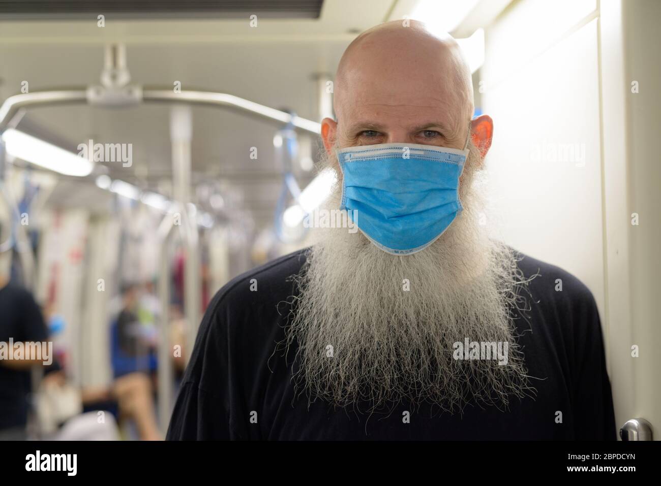 Face of mature bald bearded man with mask standing with distance inside ...