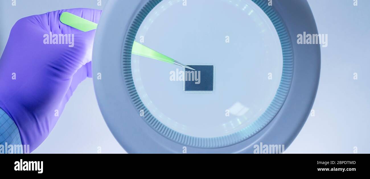 Hand in glove holding microchip with pair of tweezers under magnifying ...