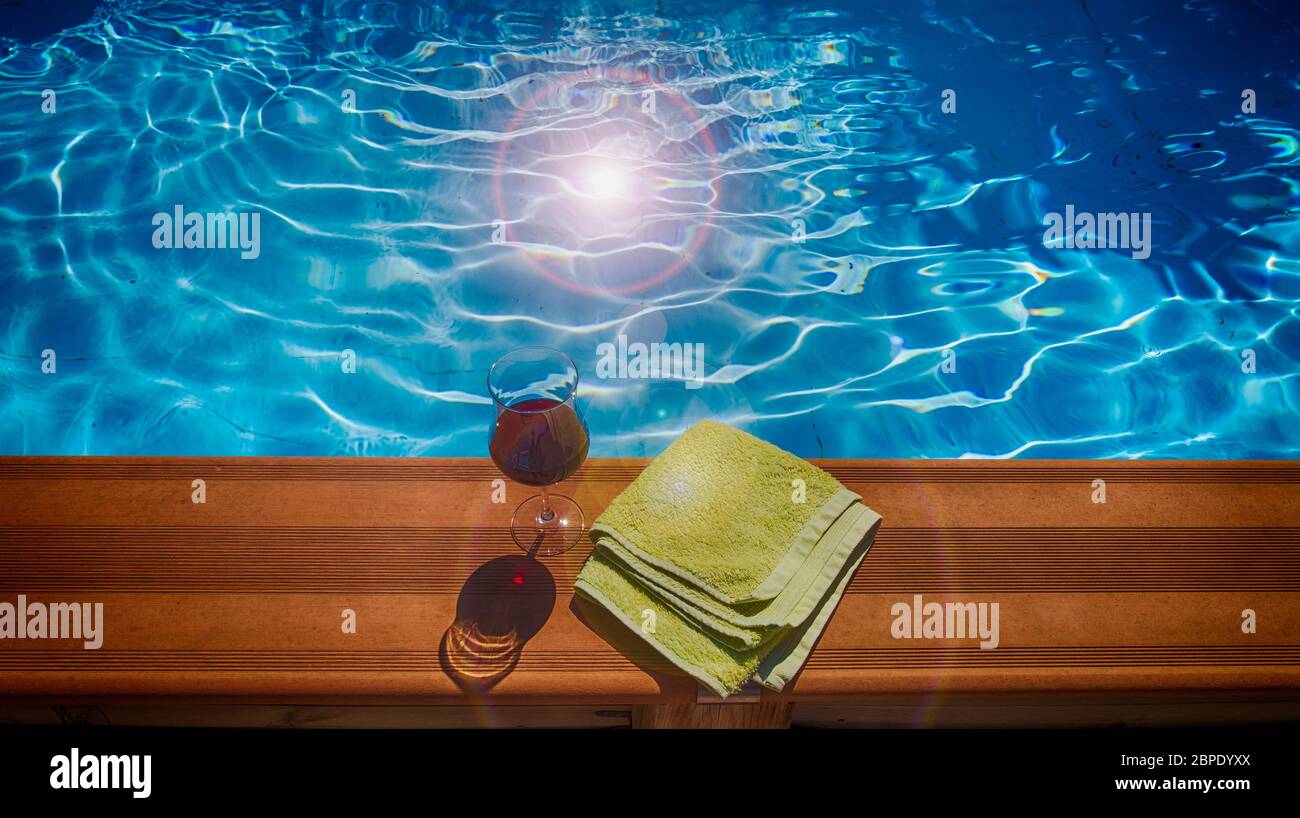 Sun flare in sunlit swimming pool with a glass of red wine and towel at ...