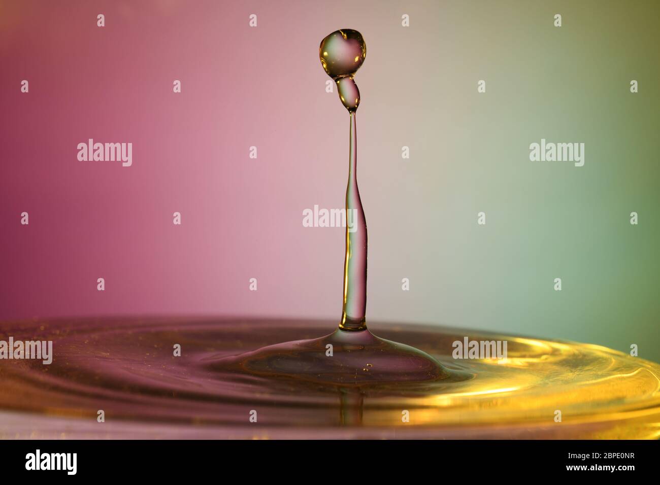 Falling water droplet against coloured background forming shape ...