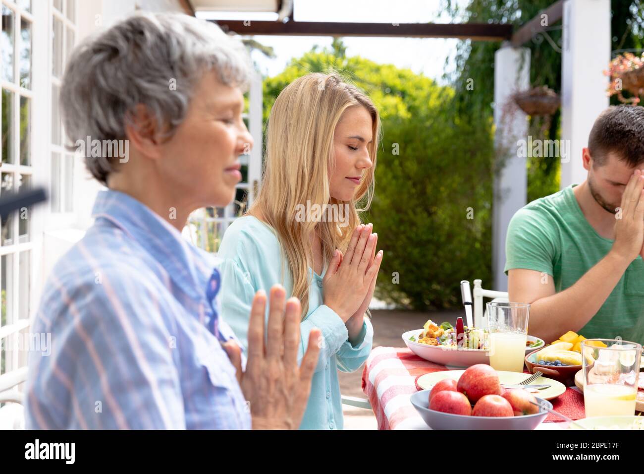 Caucasian three generation family praying during a lunch in the garden ...
