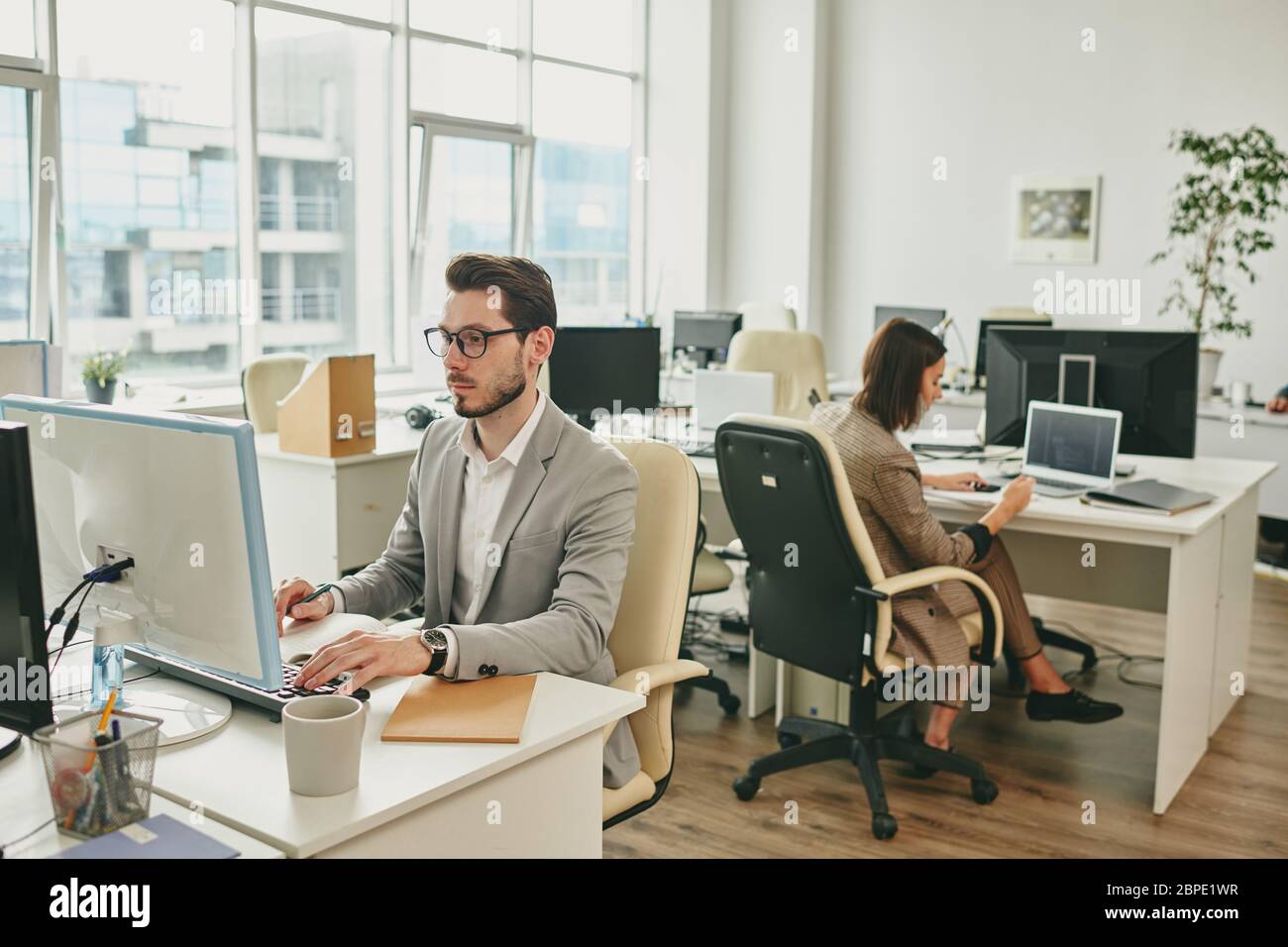 Two business people sitting at desks in office and using computers ...