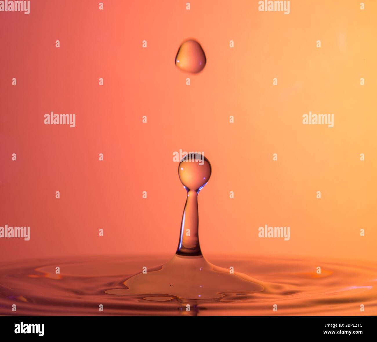 Falling water droplet against coloured background forming shape ...