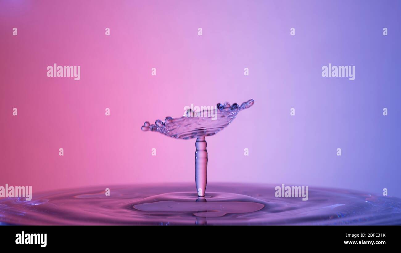 Falling water droplet against coloured background forming shape ...