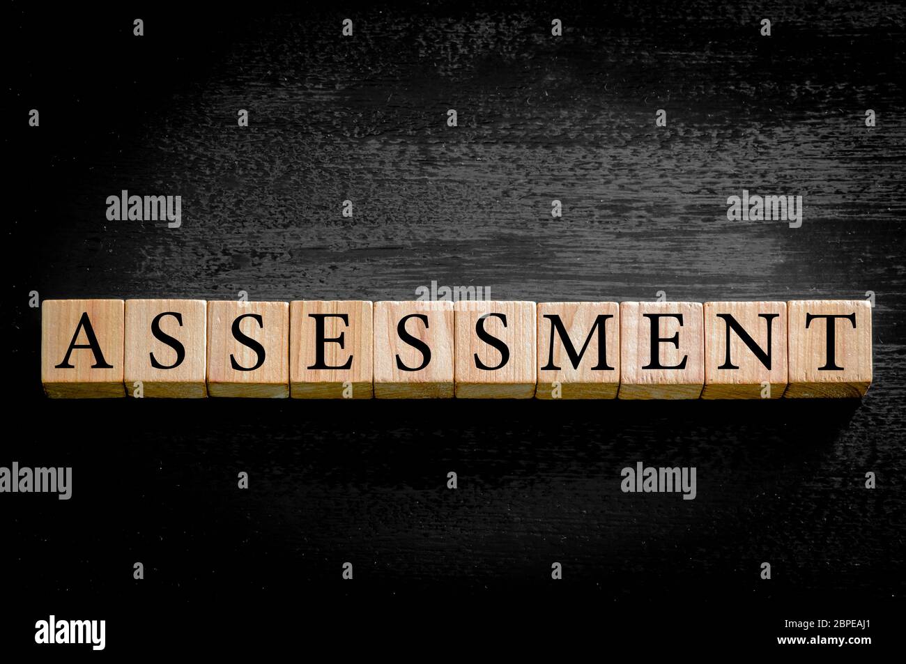 Word ASSESSMENT. Wooden small cubes with letters isolated on black ...