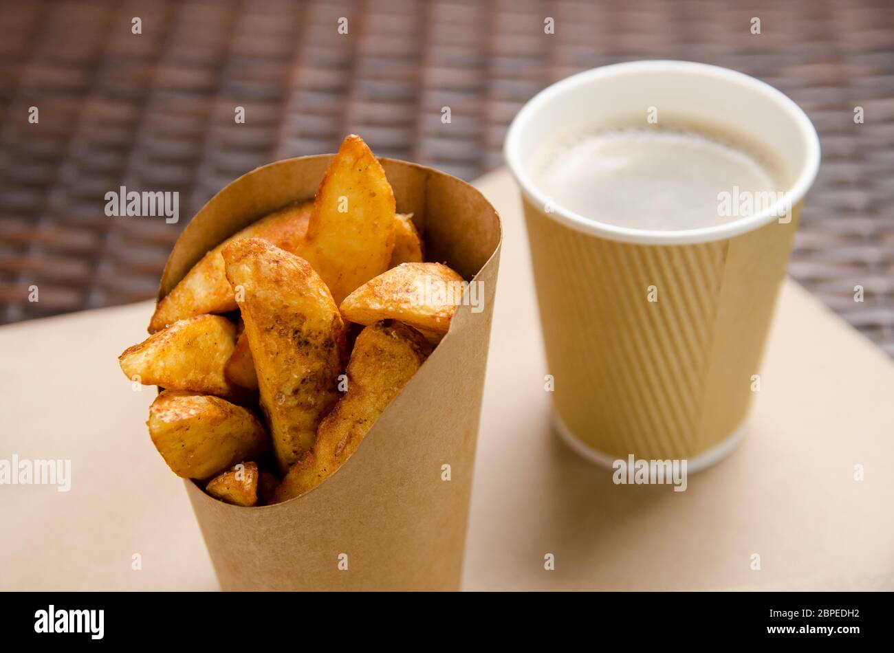 Fried potatoes in disposable packaging close-up next to coffee in a ...