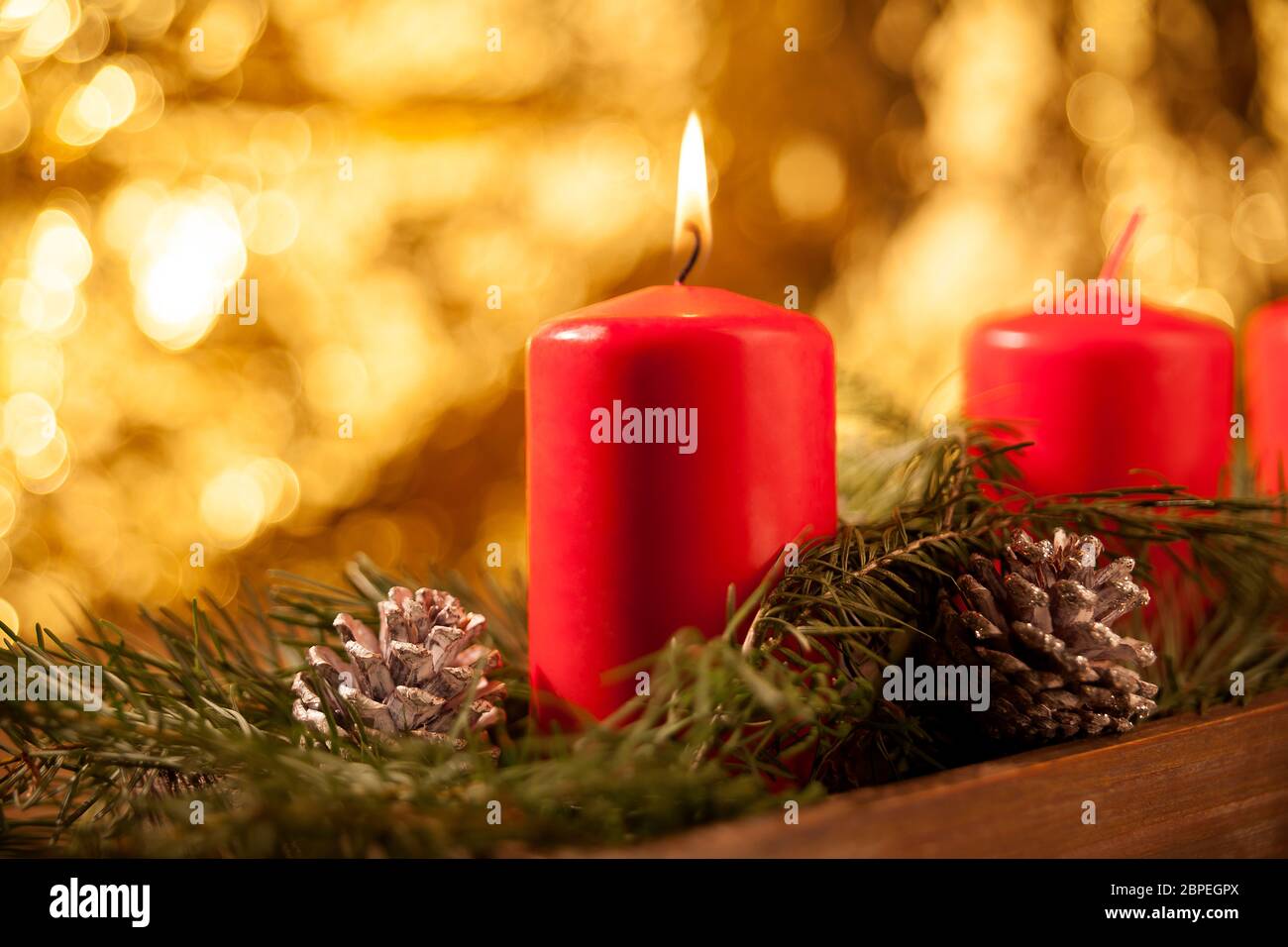 First candle burning on a red Advent wreath with golden background ...