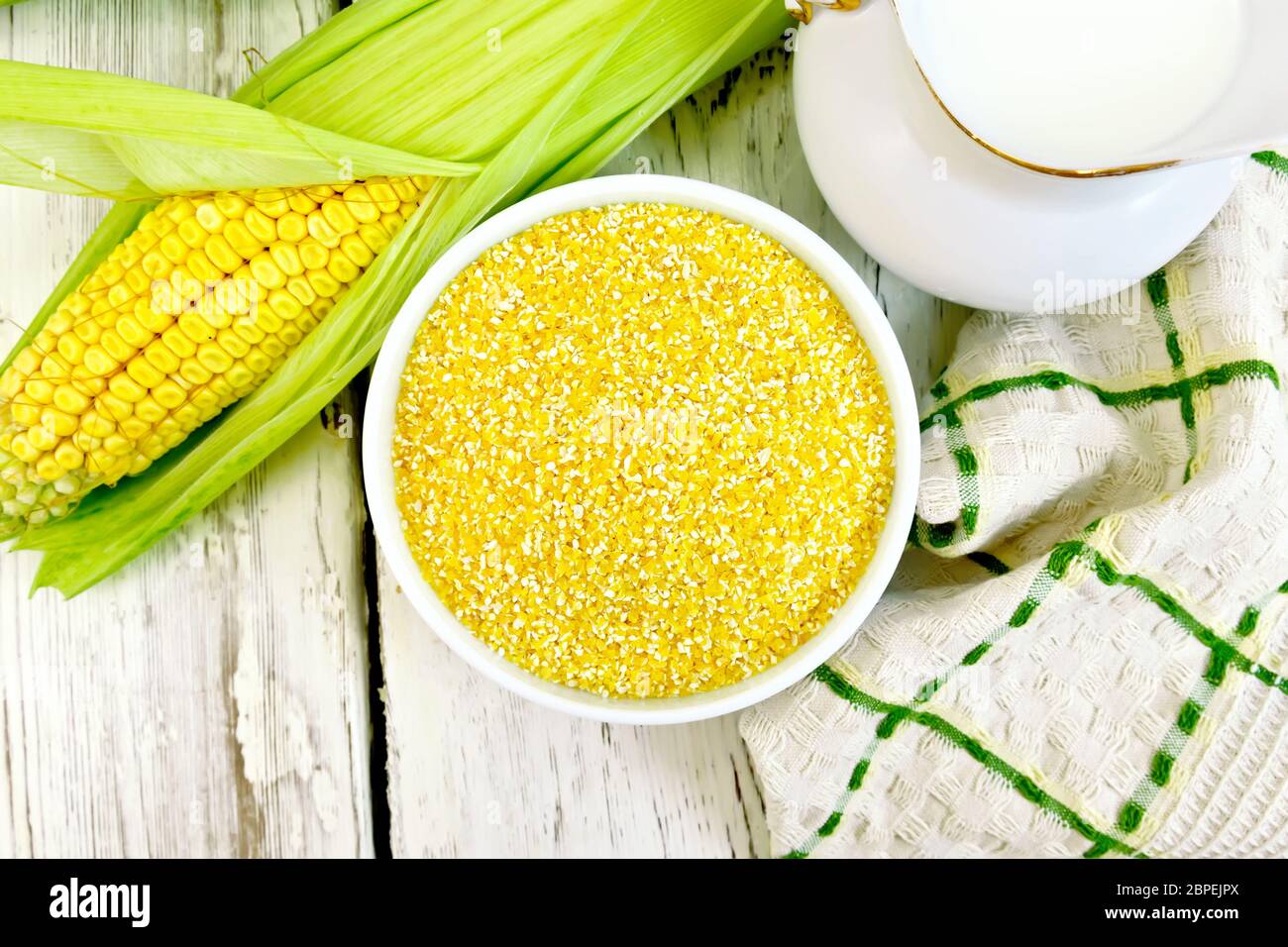 Corn grits in a white bowl, cobs, a jug of milk and a napkin on a ...