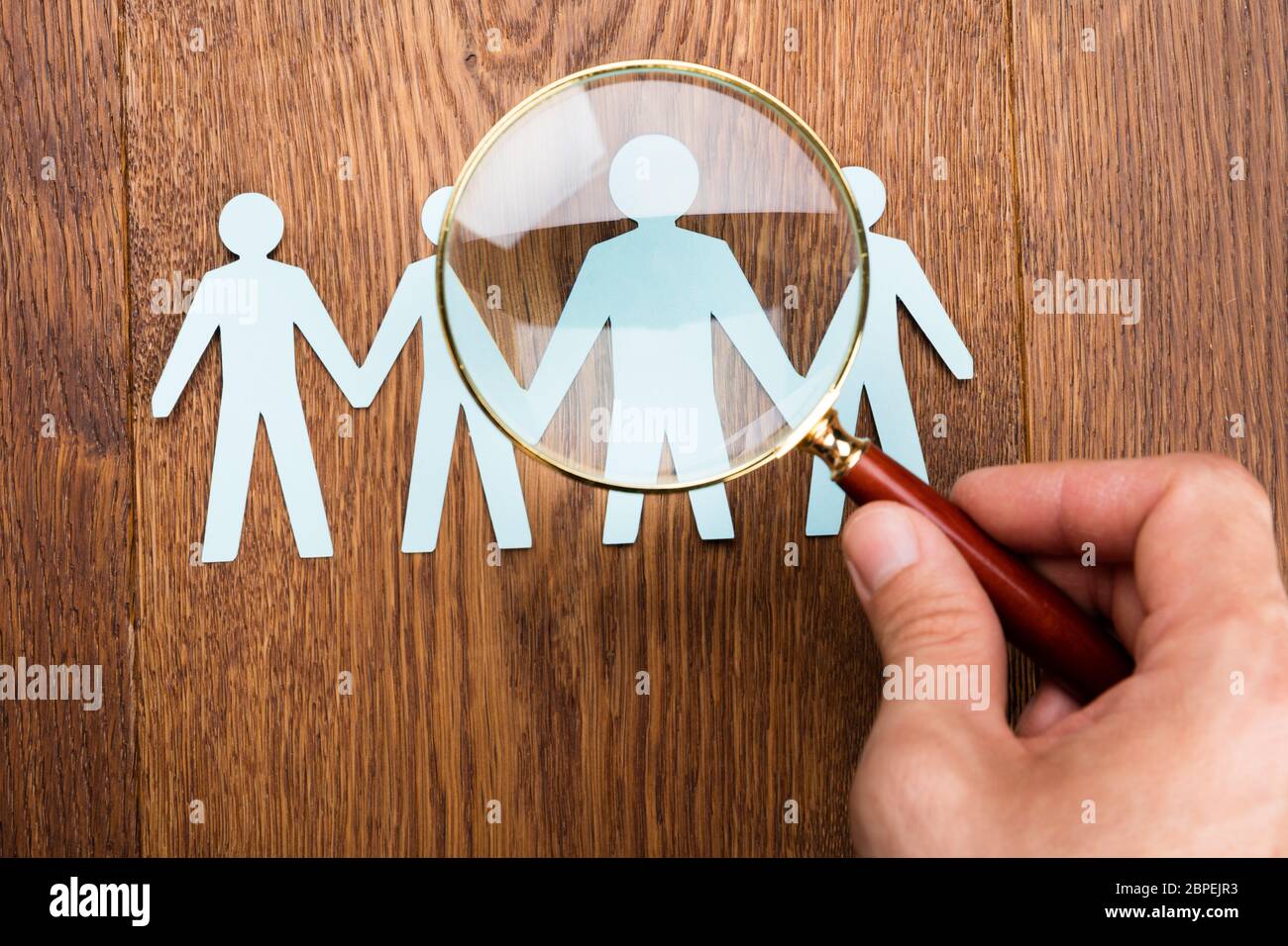 High Angle View Of Person Using Magnifying Glass On Papercut At Wooden ...