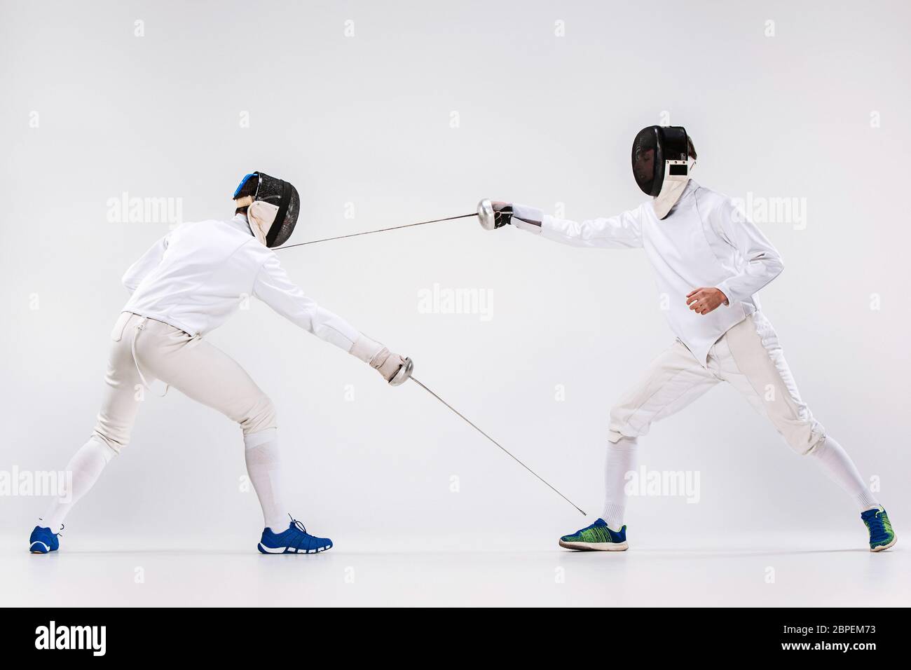 The two men wearing fencing suit practicing with sword against gray ...