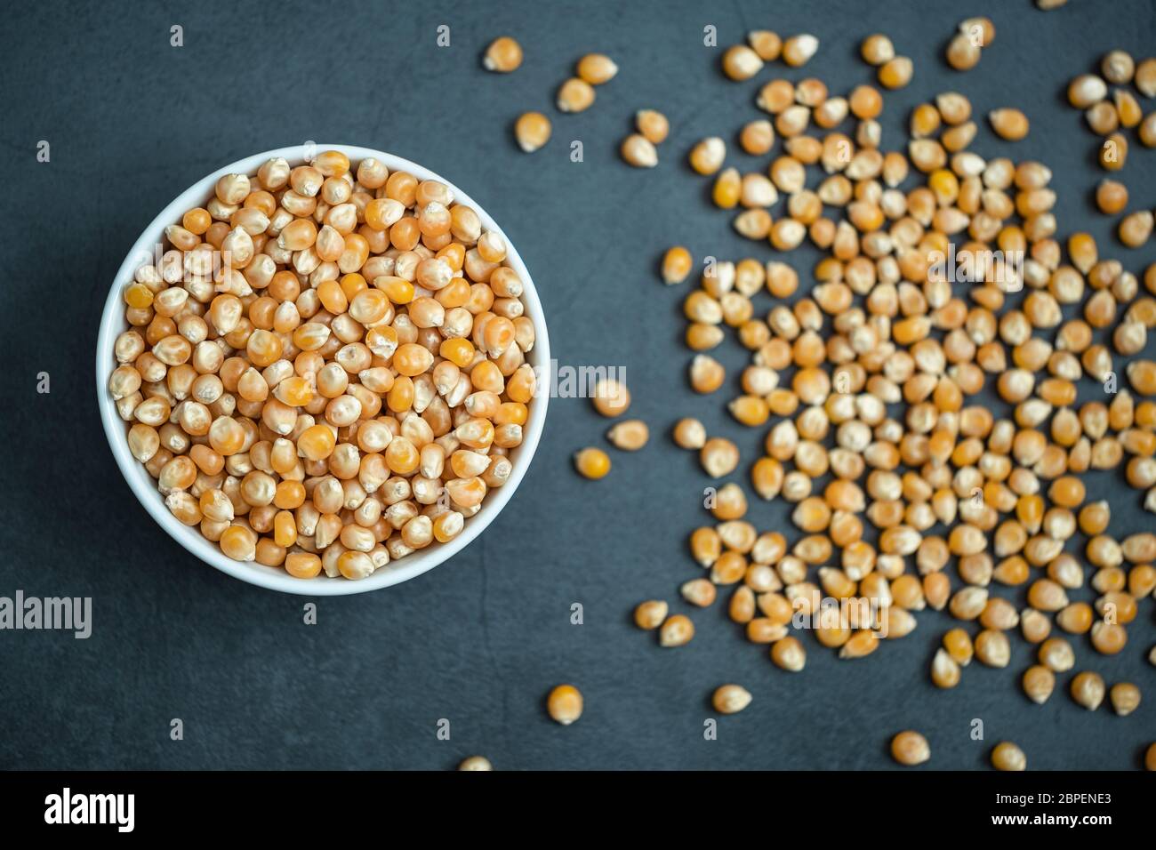 Raw corn kernel in bowl and spread around on stone, concrete background ...