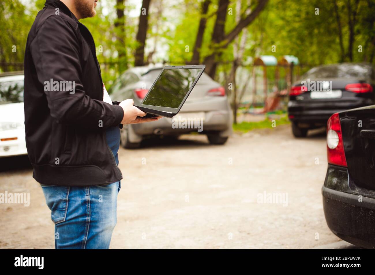 man with a laptop in parking lot in yard near car is doing ...