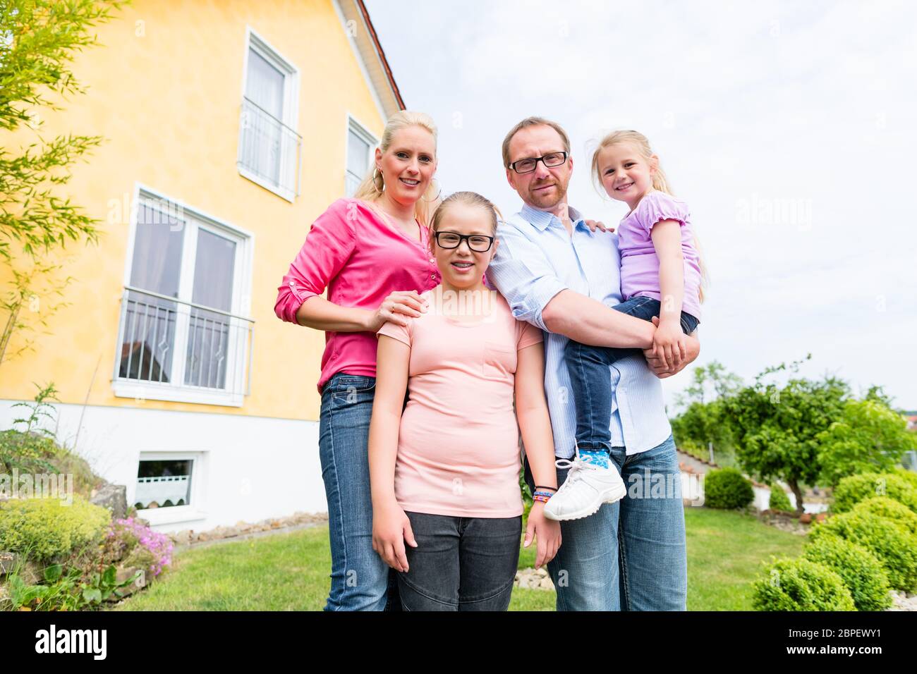 Family standing in front of home or house, mother, father and two ...