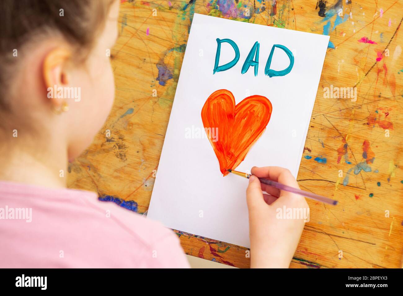 Back view of littel girl is drawing red heart with word Dad greeting ...