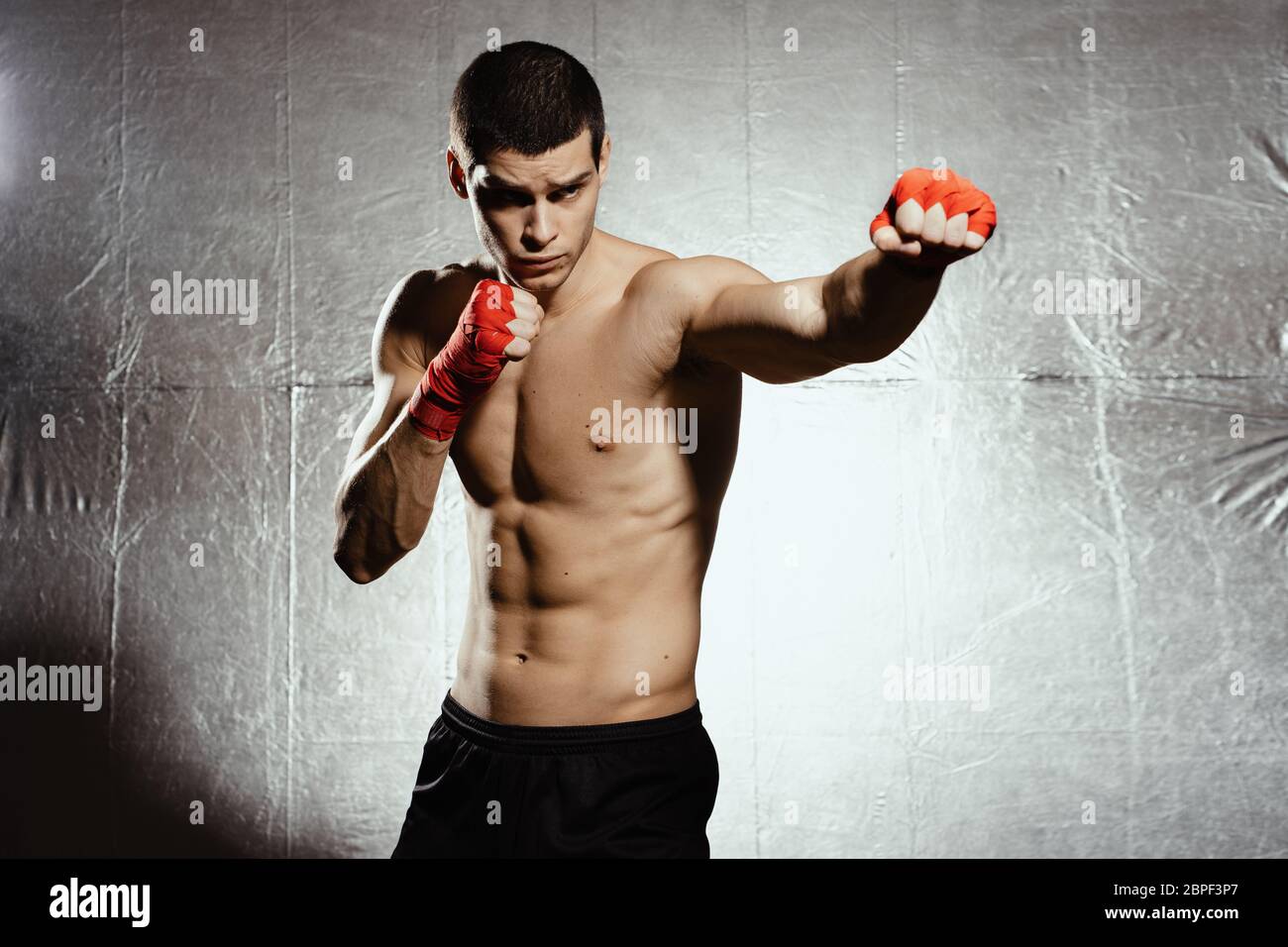 Athletic boxer punching with determination and precaution over silver ...