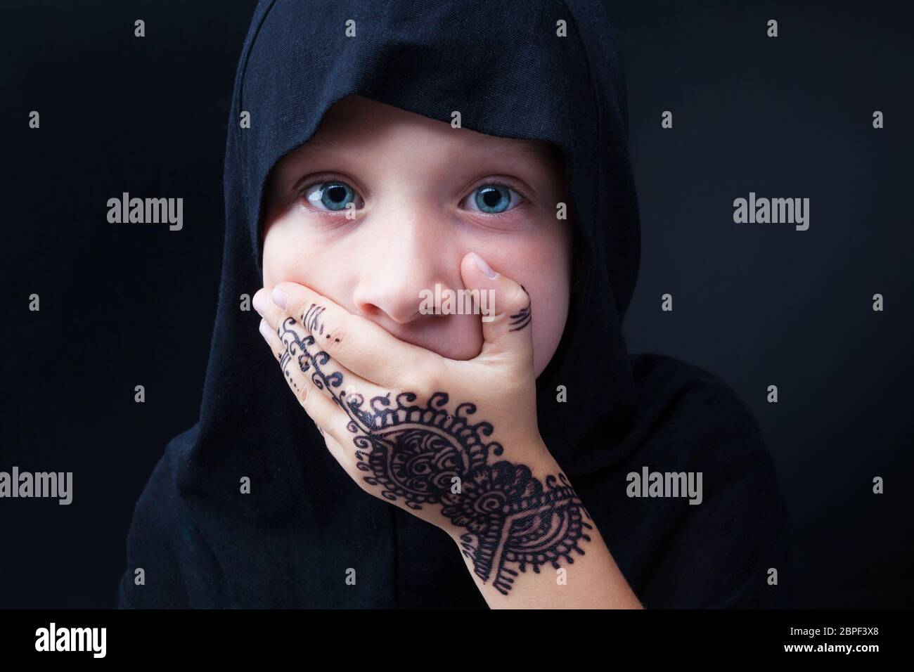 Little girl with blue eyes in muslim hijab covering mouth. Racism and ...
