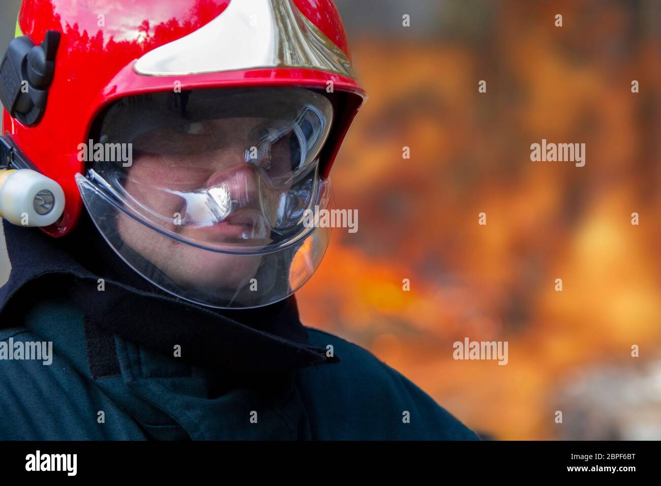 The face of a fireman in a helmet on a background of fire. Putting out ...