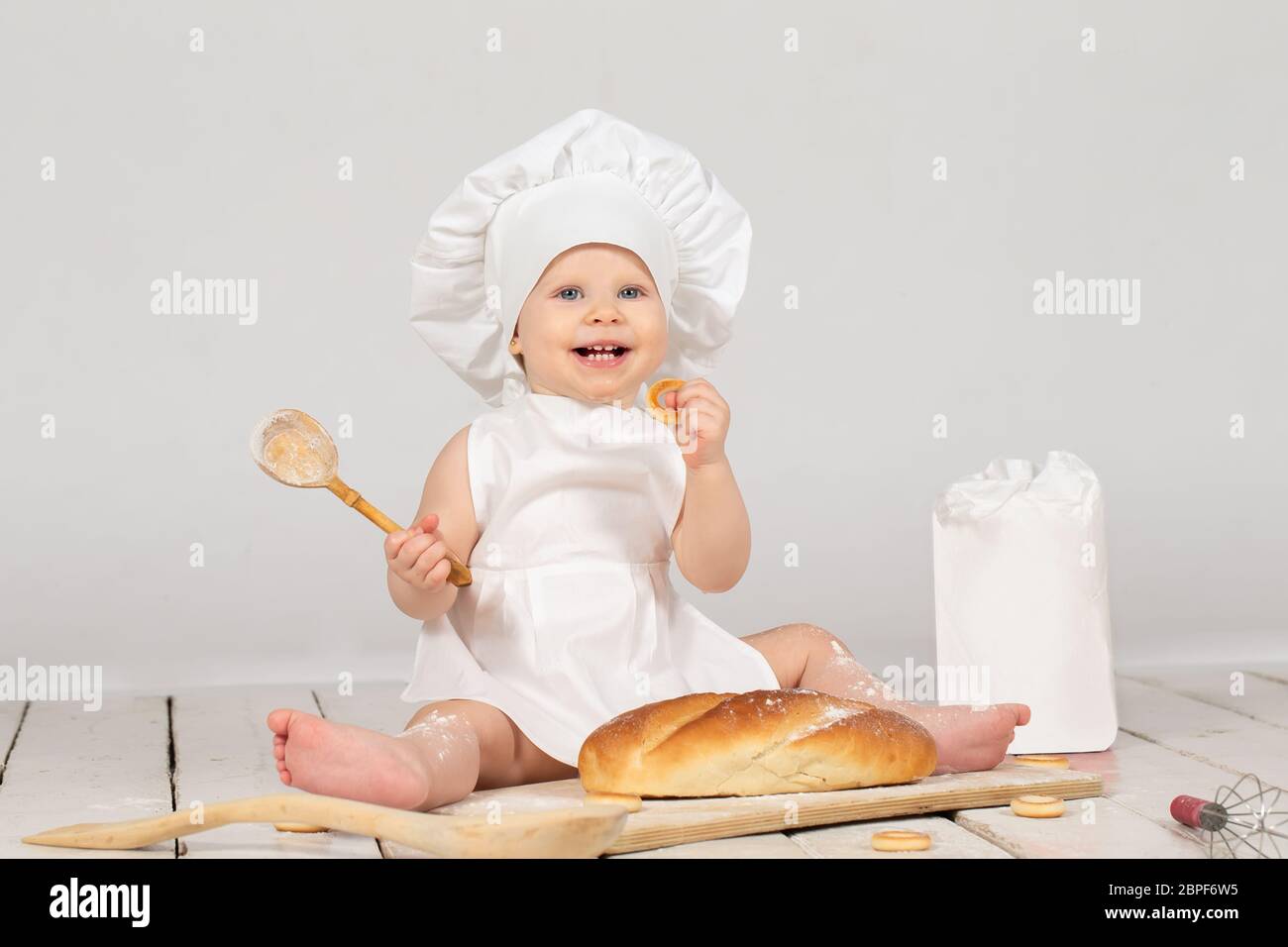 Baby cook. Beautiful little girl in cook clothes with a long loaf and a ...