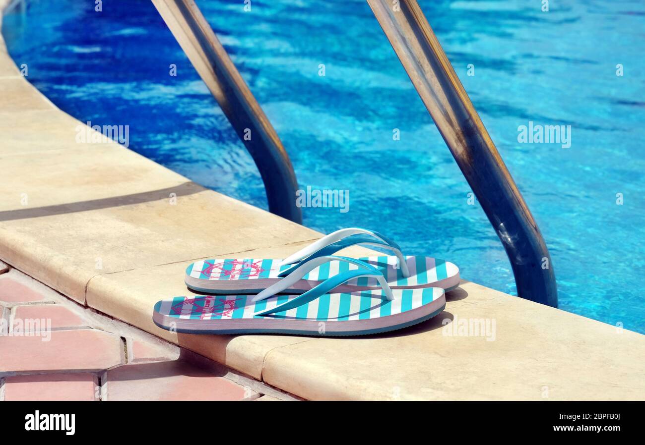 The pair of flip flops at the pool edge with clear blue water on a ...