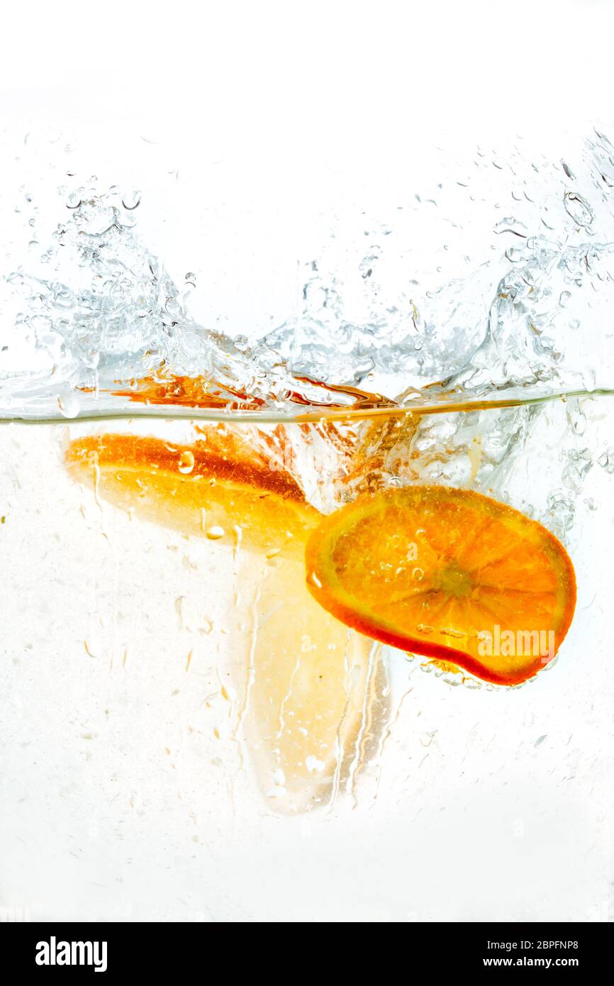 orange halves falling into water on white background Stock Photo - Alamy