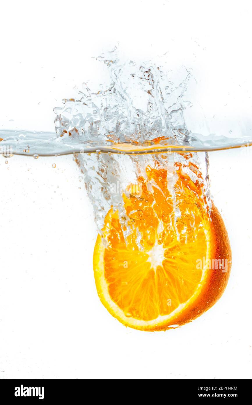 orange halves falling into water on white background Stock Photo - Alamy