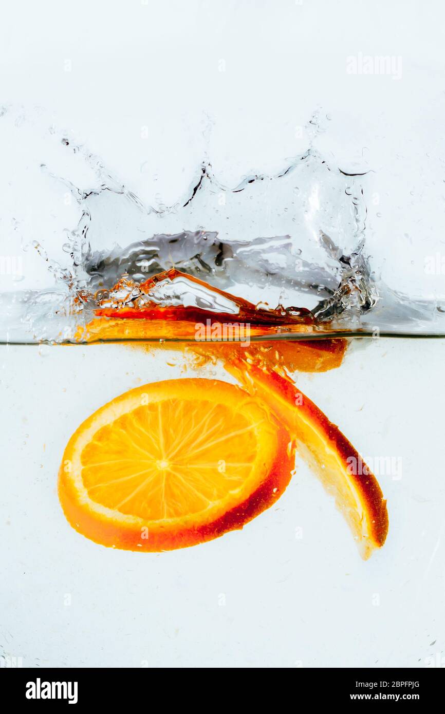 orange halves falling into water on white background Stock Photo - Alamy