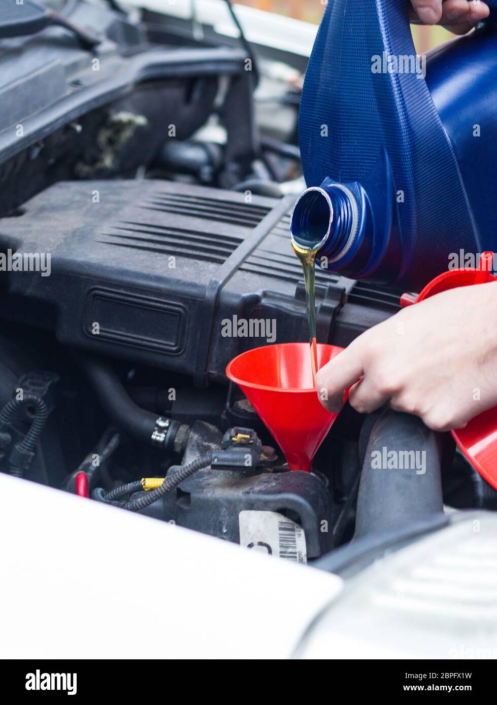 Man uses a red funnel to fill the engine oil in a car with a blue ...