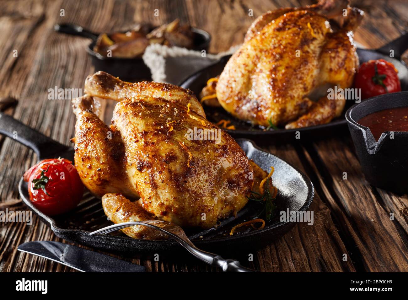 Two roasted seasoned poussin or spring chickens on skillets with ...