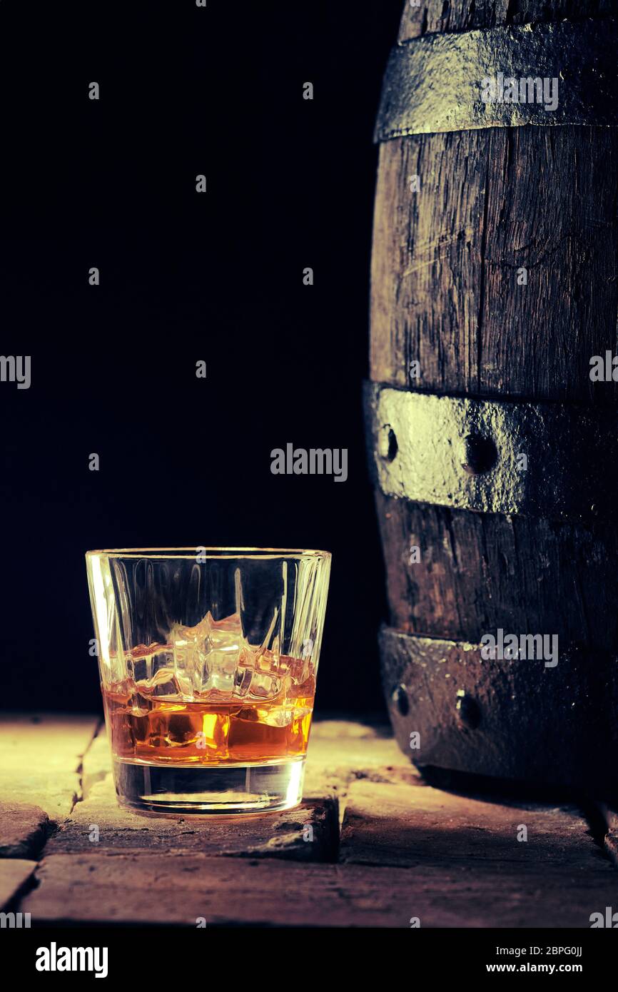 Glass of scotch on the rocks alongside an old oak barrel viewed side on ...
