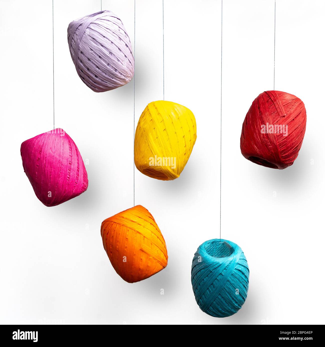 some colored raffia balls hanging from a white surface Stock Photo - Alamy