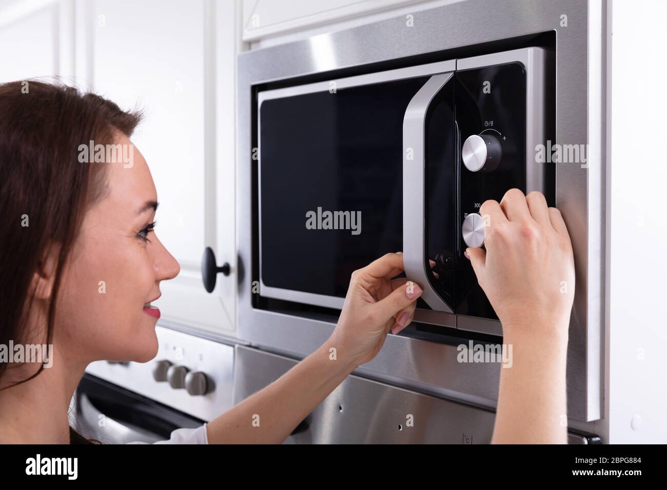 Side View Of A Young Woman Using Microwave Oven In Kitchen Stock Photo ...