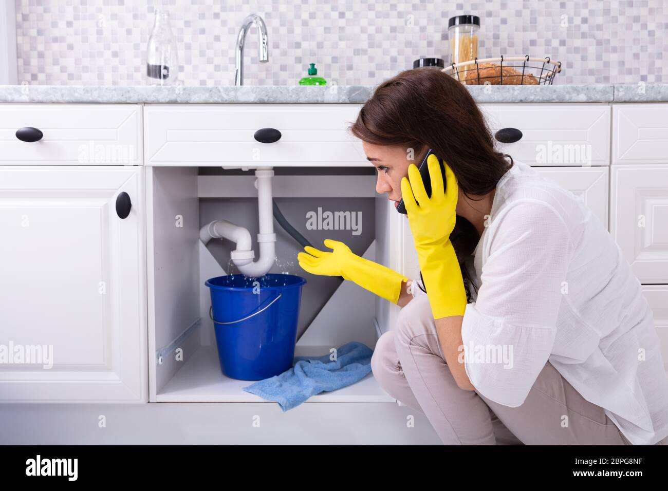 Sad Young Woman Calling Plumber In Front Of Water Leaking From Sink ...