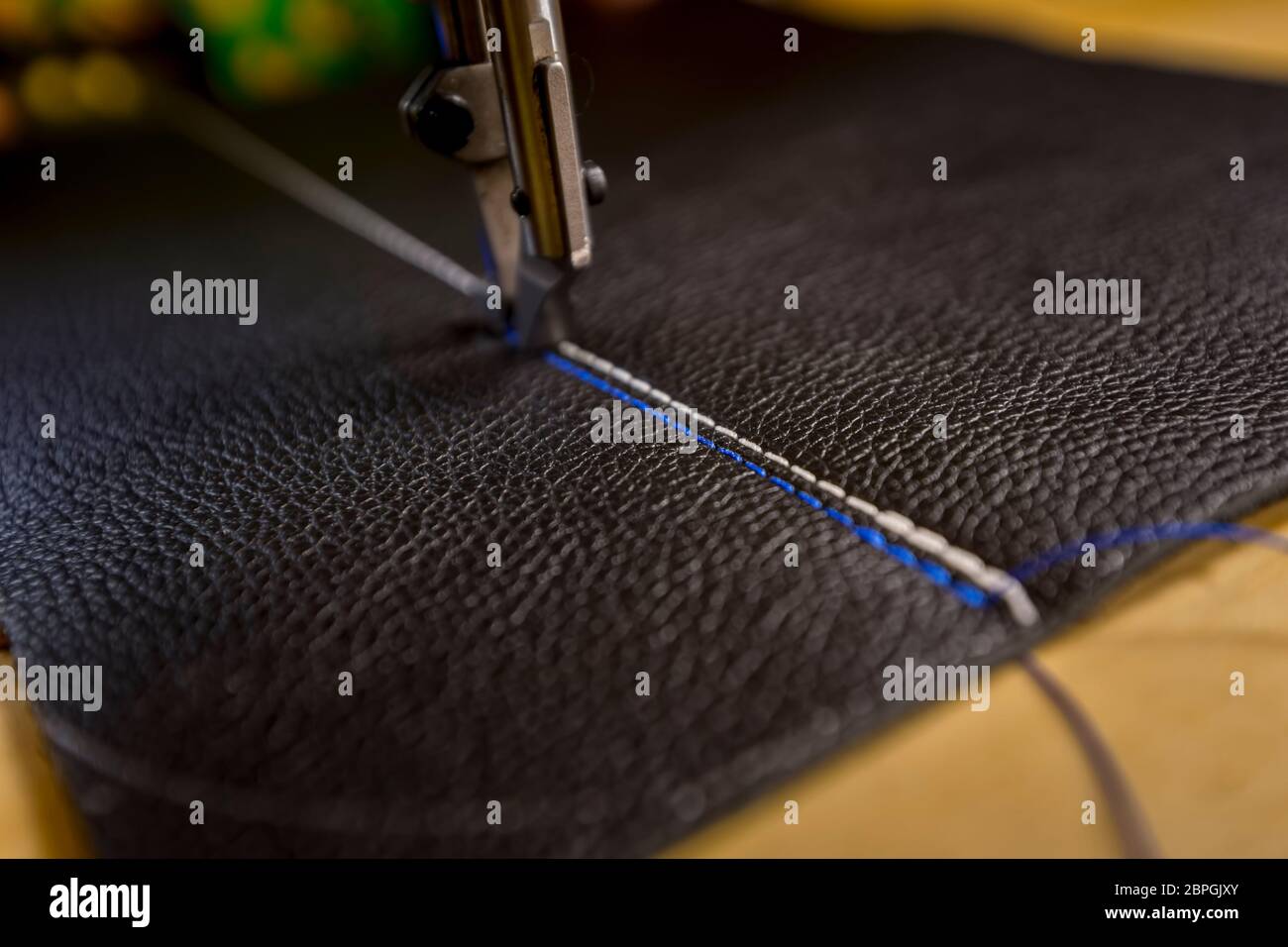 Black leather on industrial sewing machine with white and blue stitches ...
