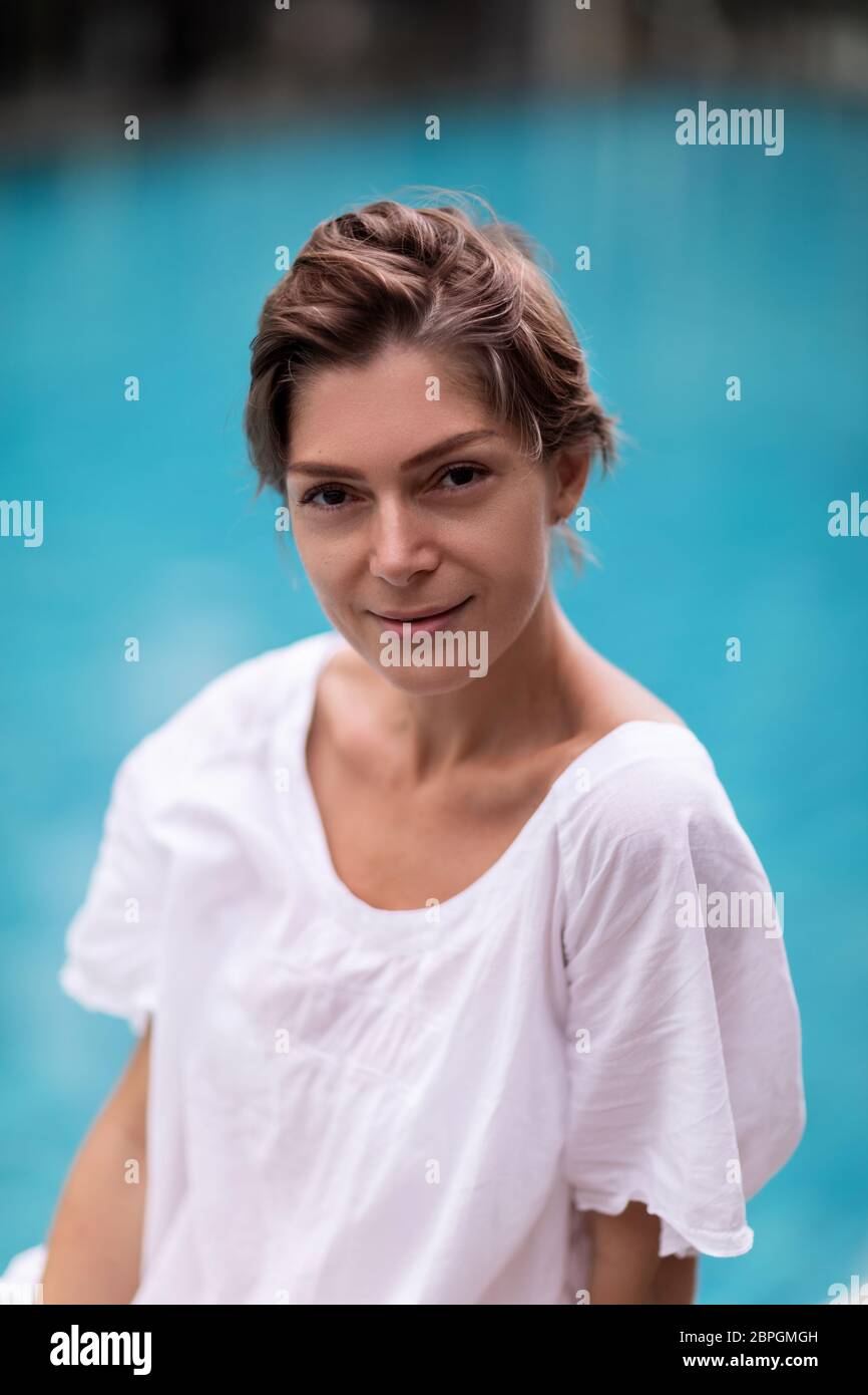Pretty slim woman with sort haircut sitting near pool outdoors in ...