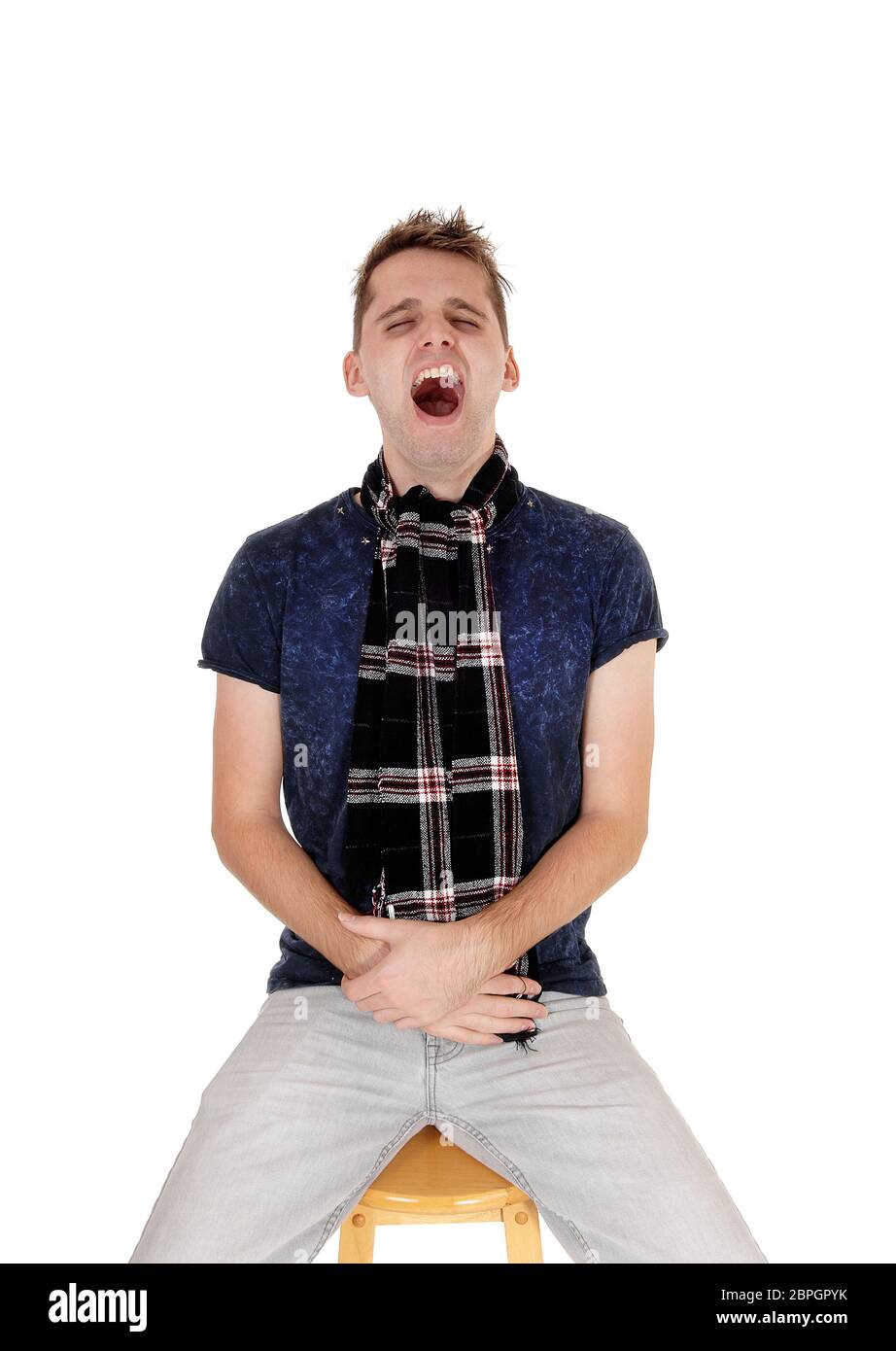 A very tired young man sitting on a chair with a scarf around his neck ...