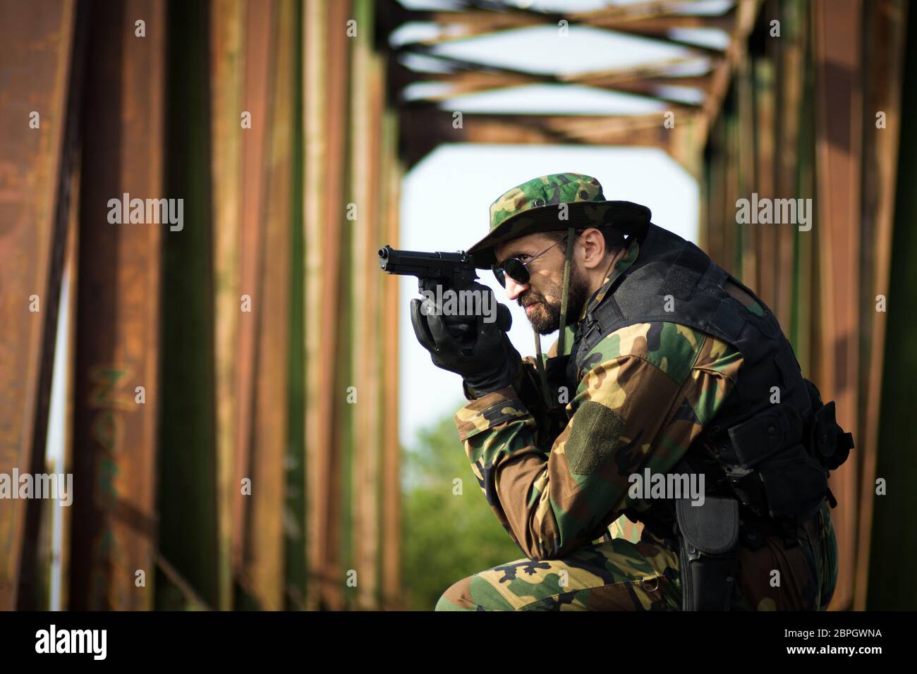 The army soldier in military uniform is aiming with pistol outdoors on ...