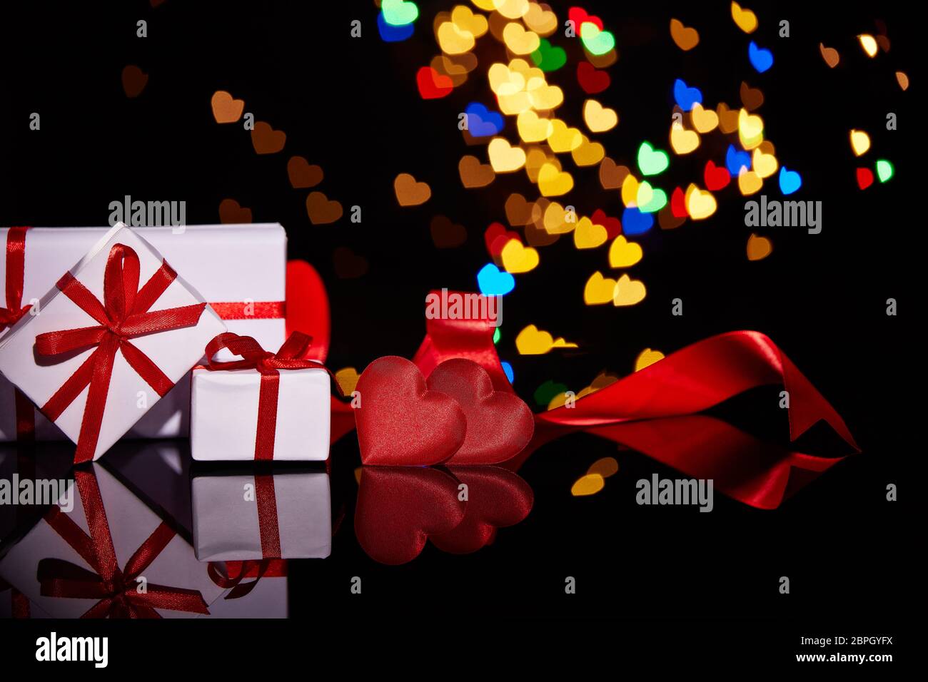 Gift boxes and red satin hearts on a black background with heart-shaped ...