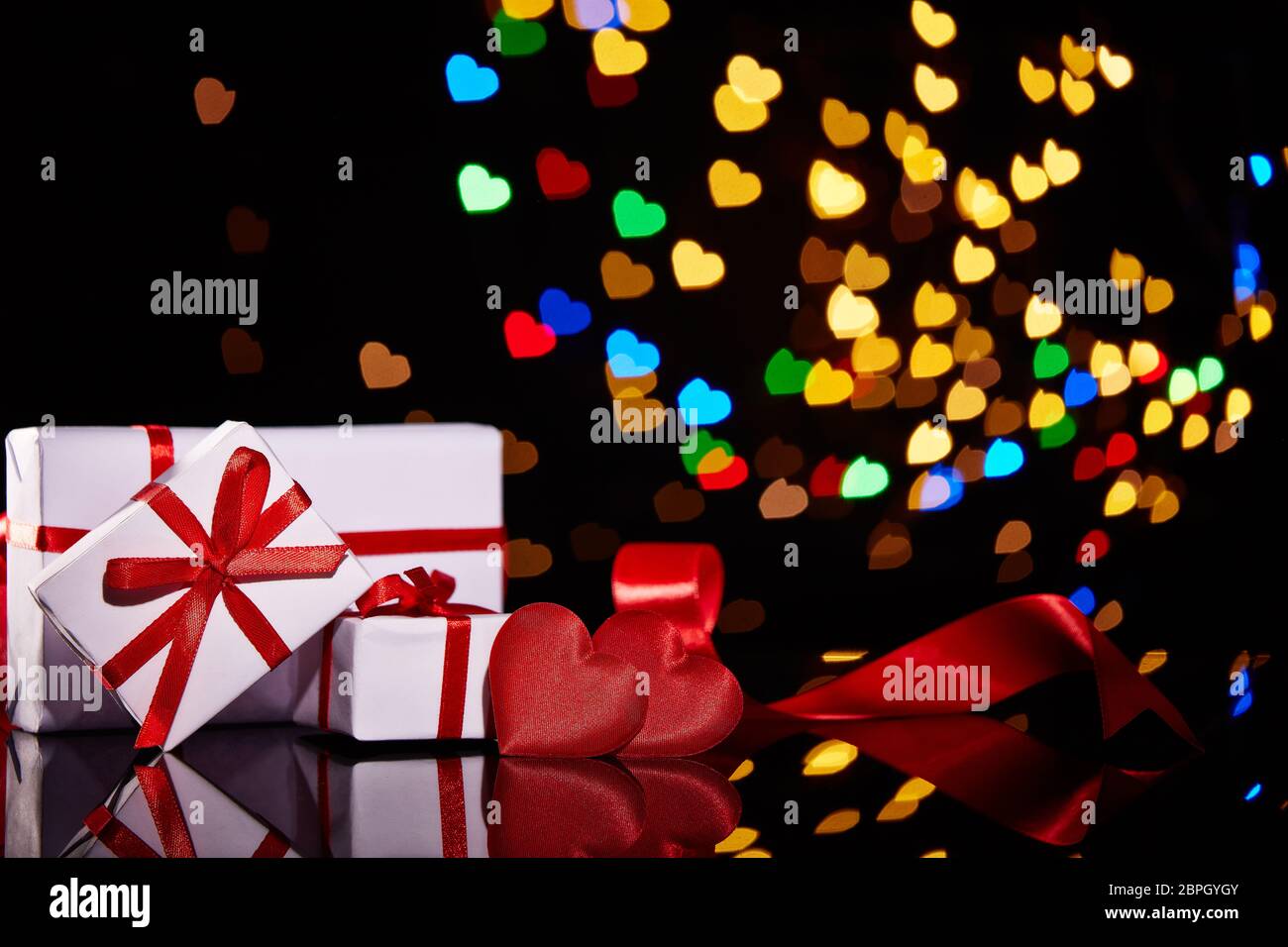 Gift boxes and red satin hearts on a black background with heart-shaped ...