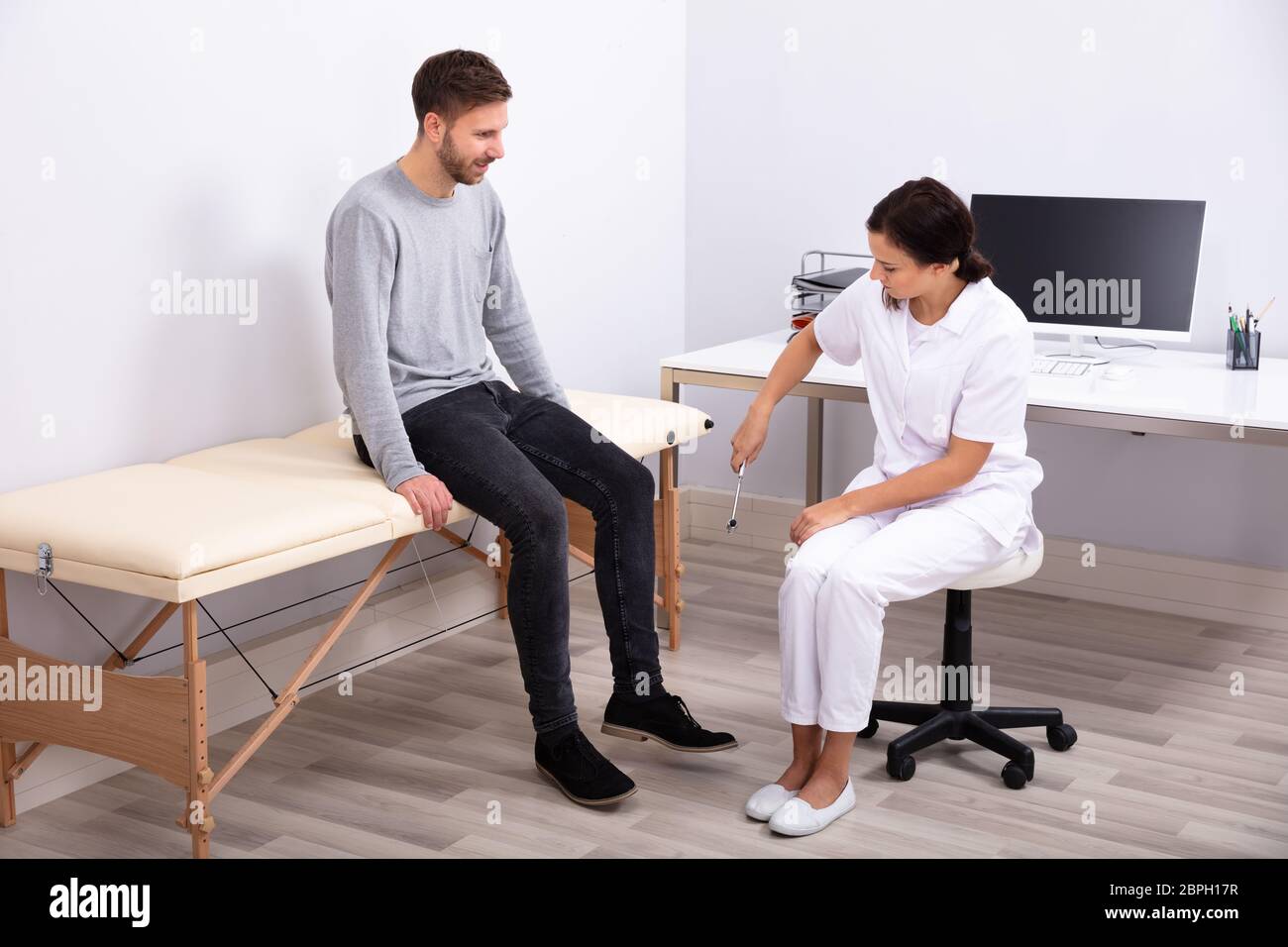 Young Female Doctor Checking Knee Reflexes Of Male Patient With Reflex ...