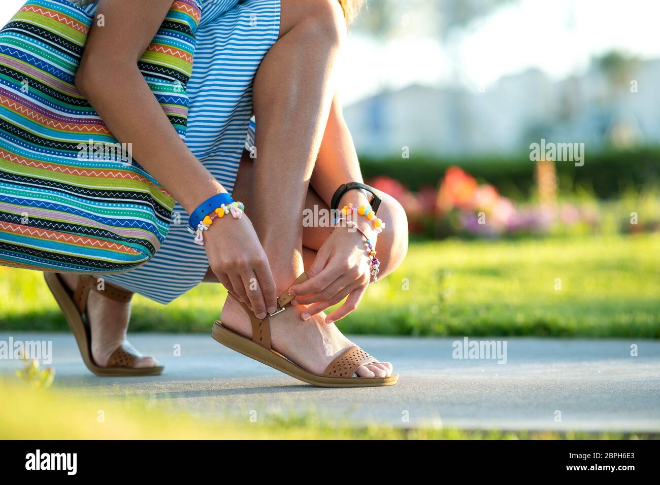 Close up of woman hands tying her open summer sandals shoes on sidewalk ...