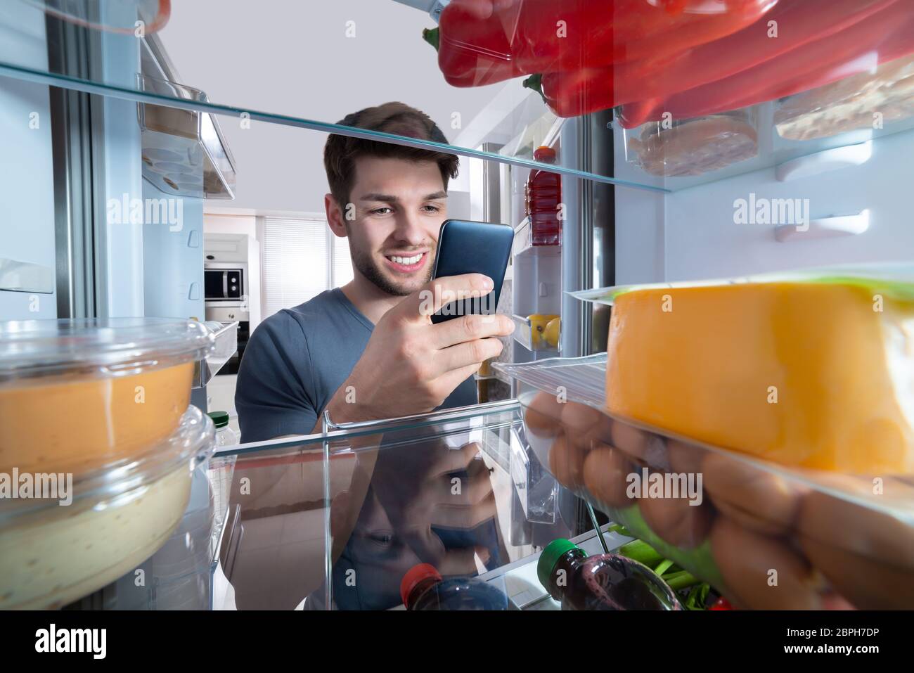 Happy Man Standing In Front Of Refrigerator Using Mobilephone In ...