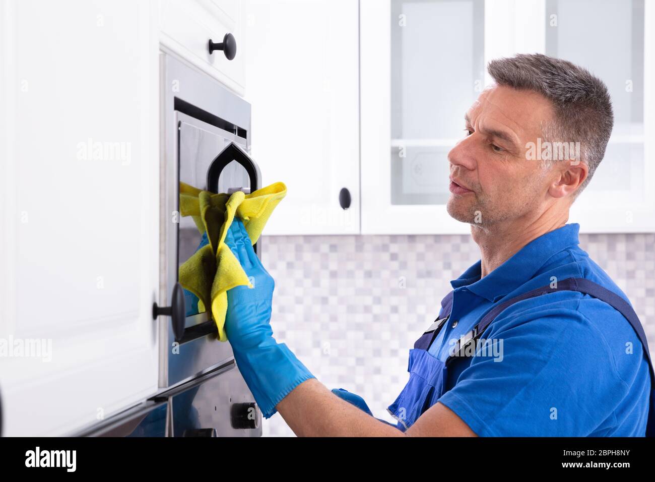Side View Of Male Janitor Cleaning Oven With Yellow Napkin In Kitchen ...