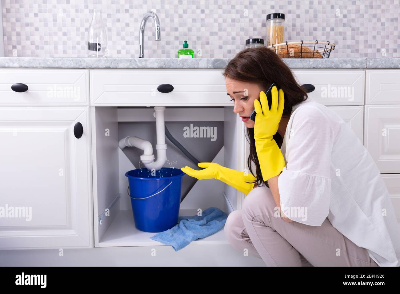 Sad Young Woman Calling Plumber In Front Of Water Leaking From Sink ...